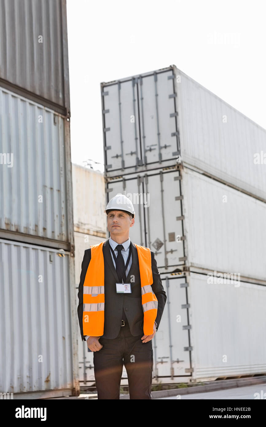 Middle-aged man standing against cargo containers in shipping yard ...