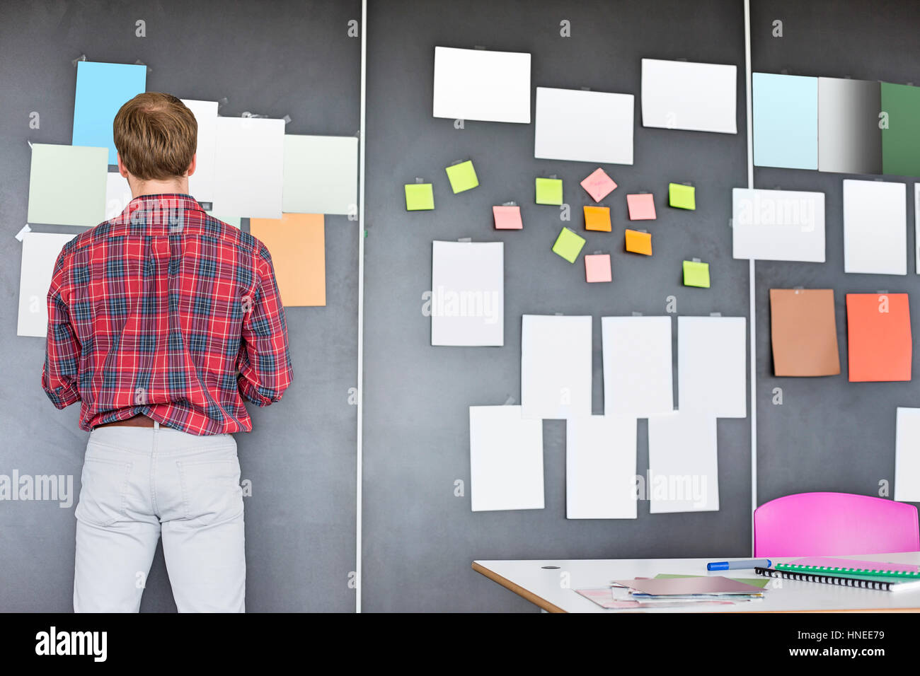 Rear view of businessman analyzing documents on wall at creative office ...