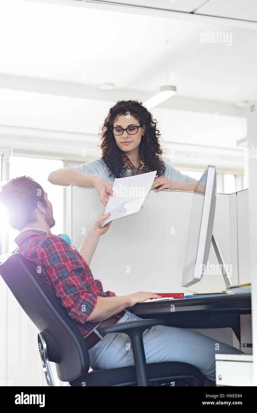 Businessman handing over document to female colleague over cubicle wall ...