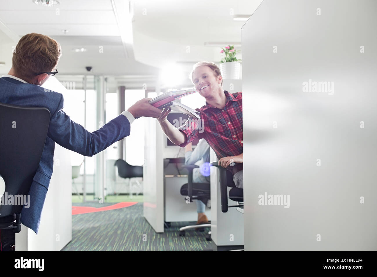 Rear view of businessman giving files to colleague in creative office ...