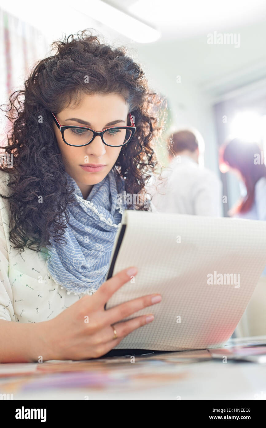 Young businesswoman reading notepad at creative office with colleagues ...