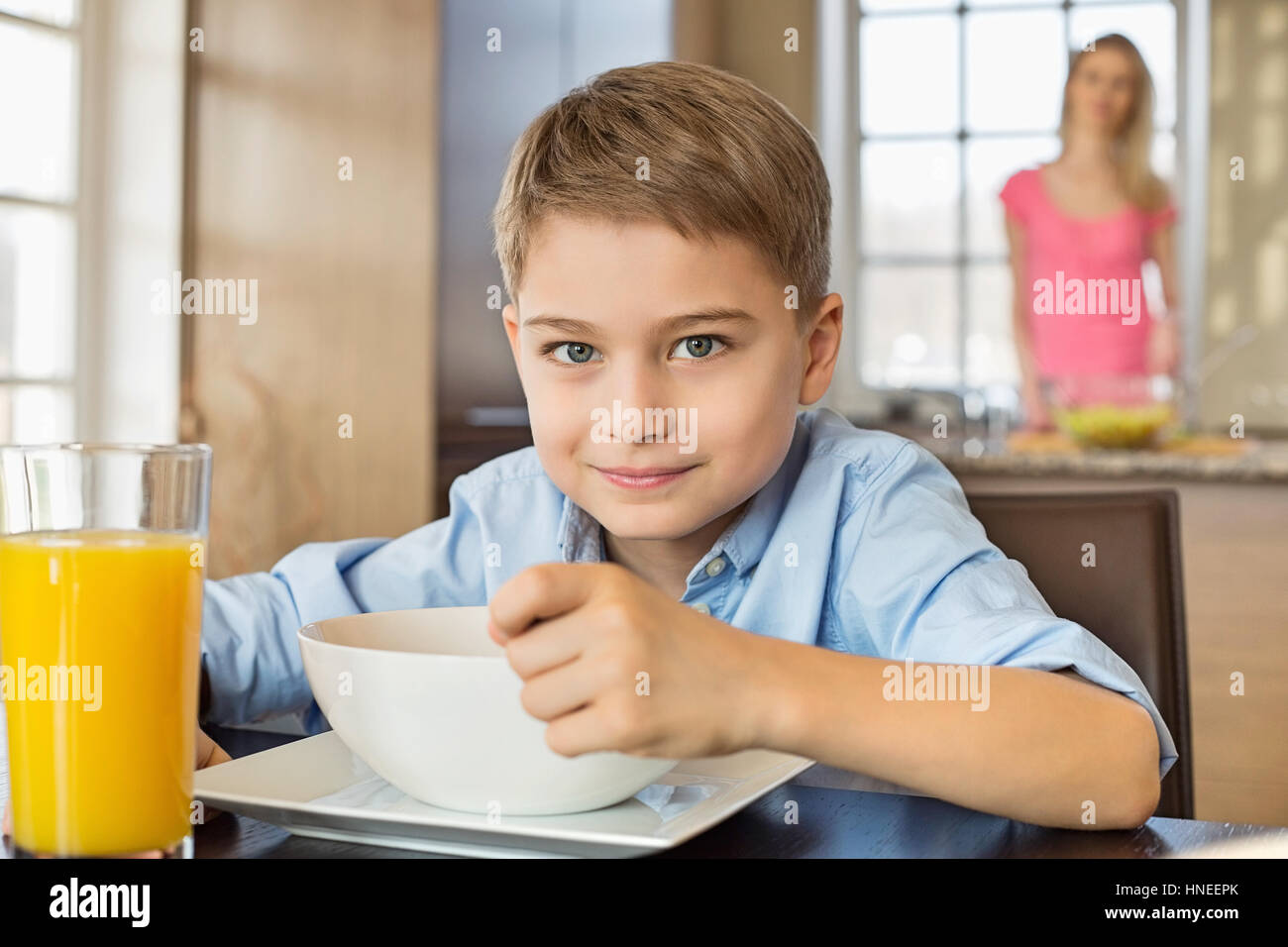 Portrait of boy having breakfast at table with mother standing in ...