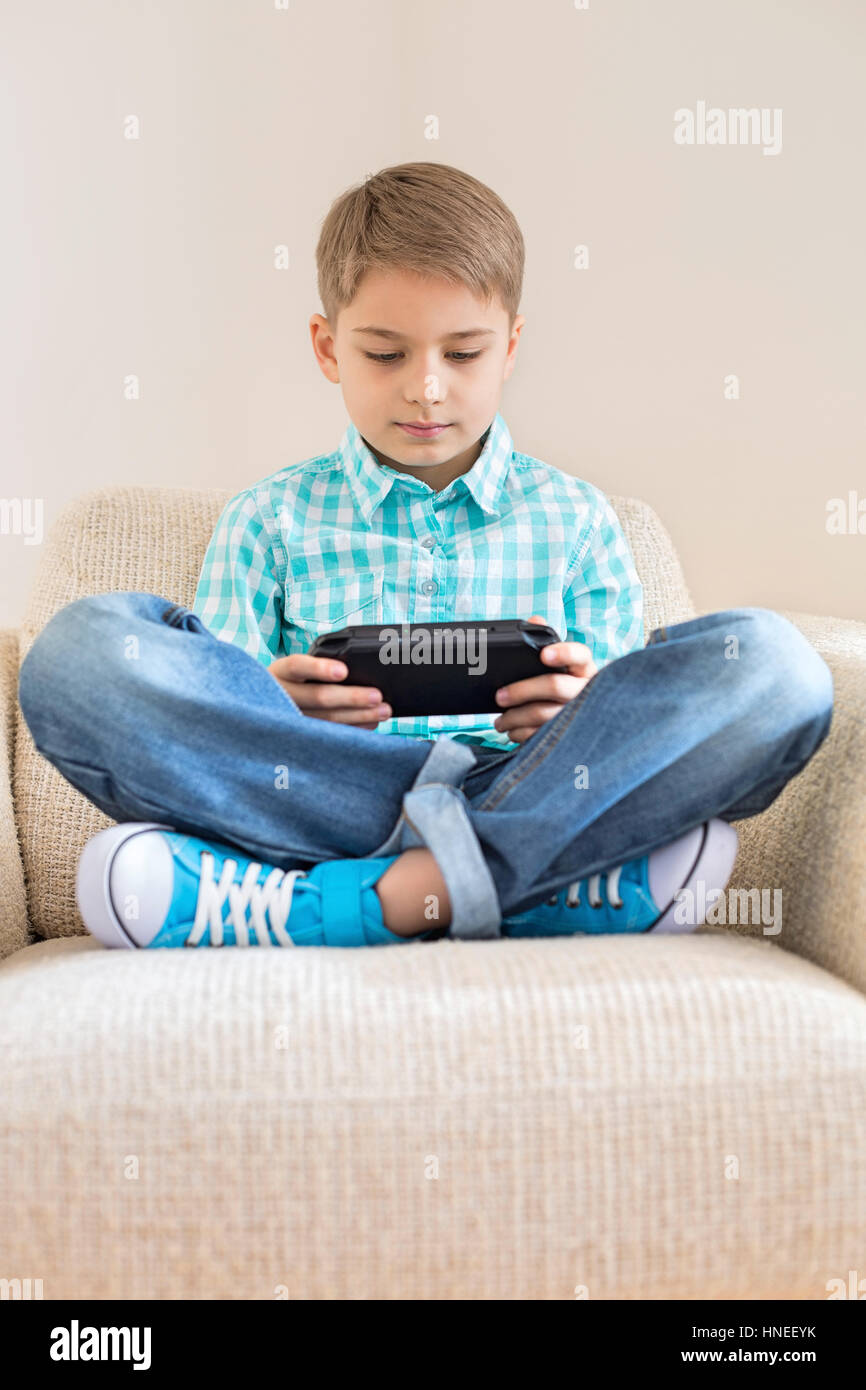 Boy playing hand-held video game on sofa at home Stock Photo - Alamy