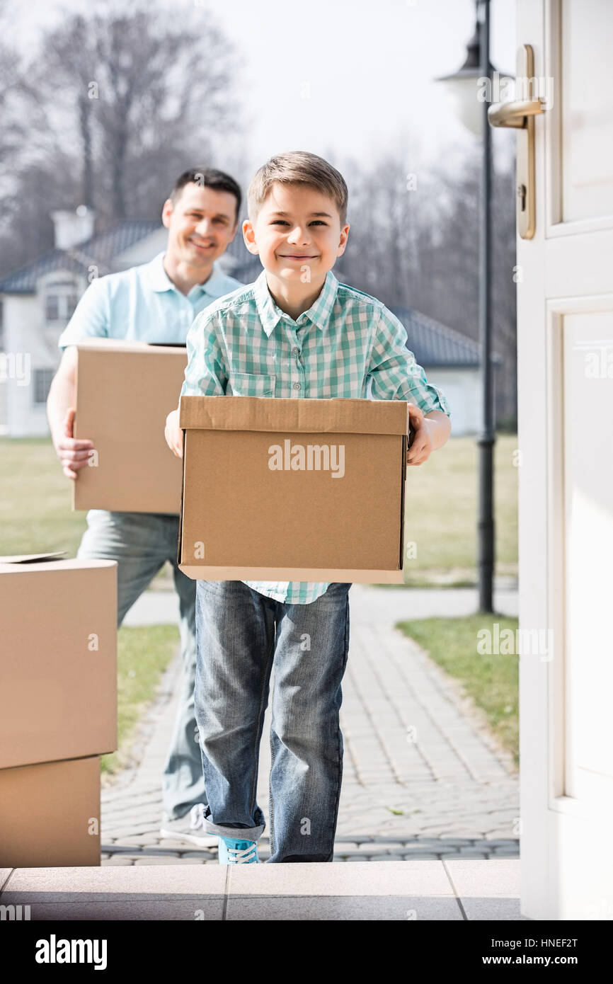 Happy father and son with cardboard boxes entering new home Stock Photo ...