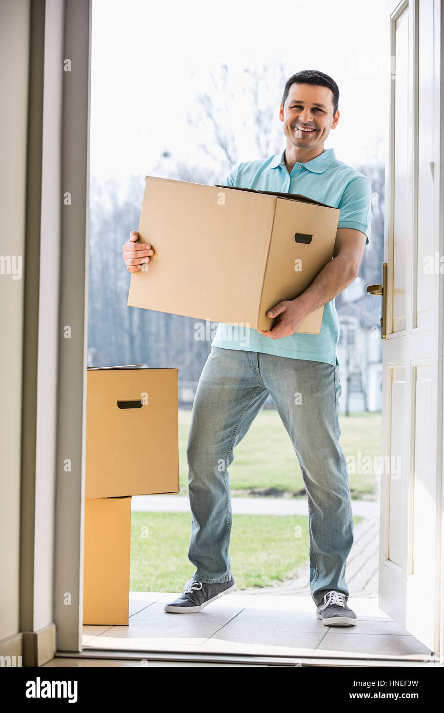 Portrait of happy man carrying cardboard box while entering new home ...