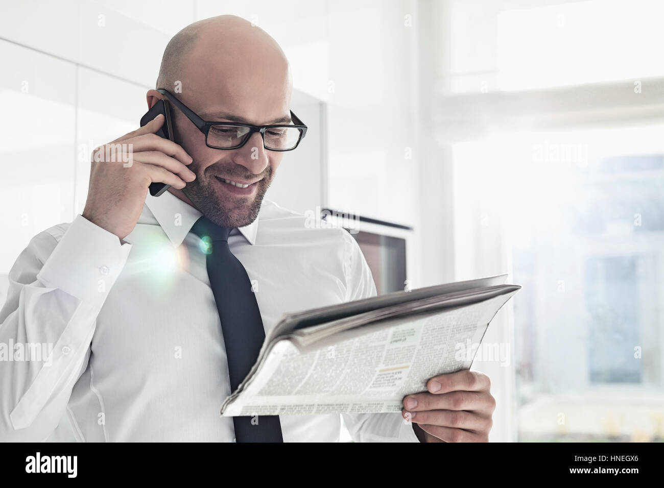 Happy businessman on call while reading newspaper at home Stock Photo ...