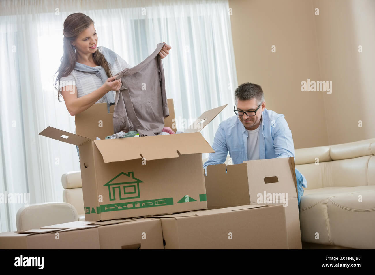 Mid-adult couple unpacking cardboard boxes in new home Stock Photo - Alamy