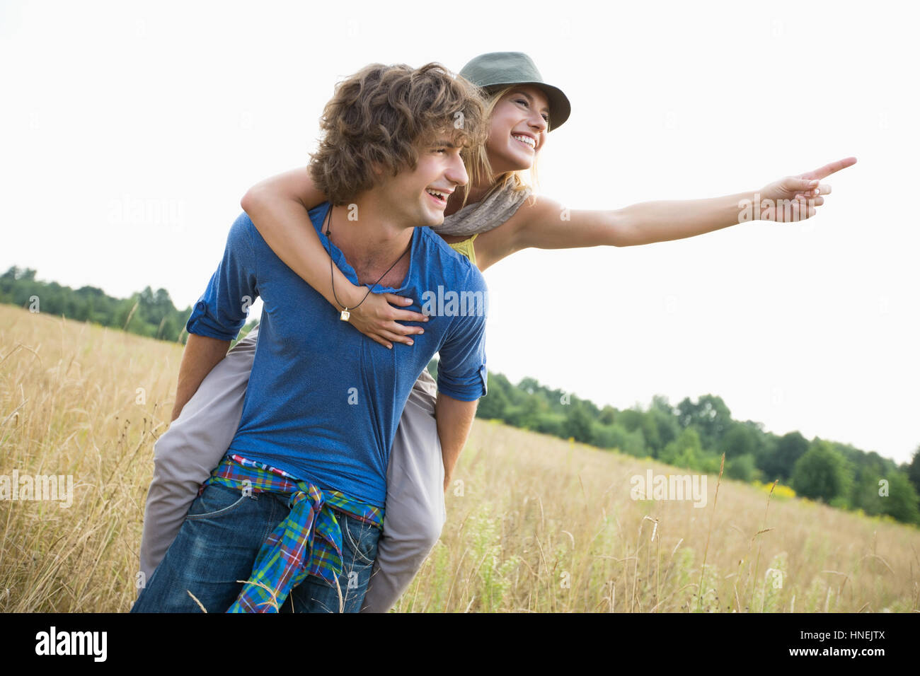 Woman showing something while enjoying piggyback ride on man in field ...