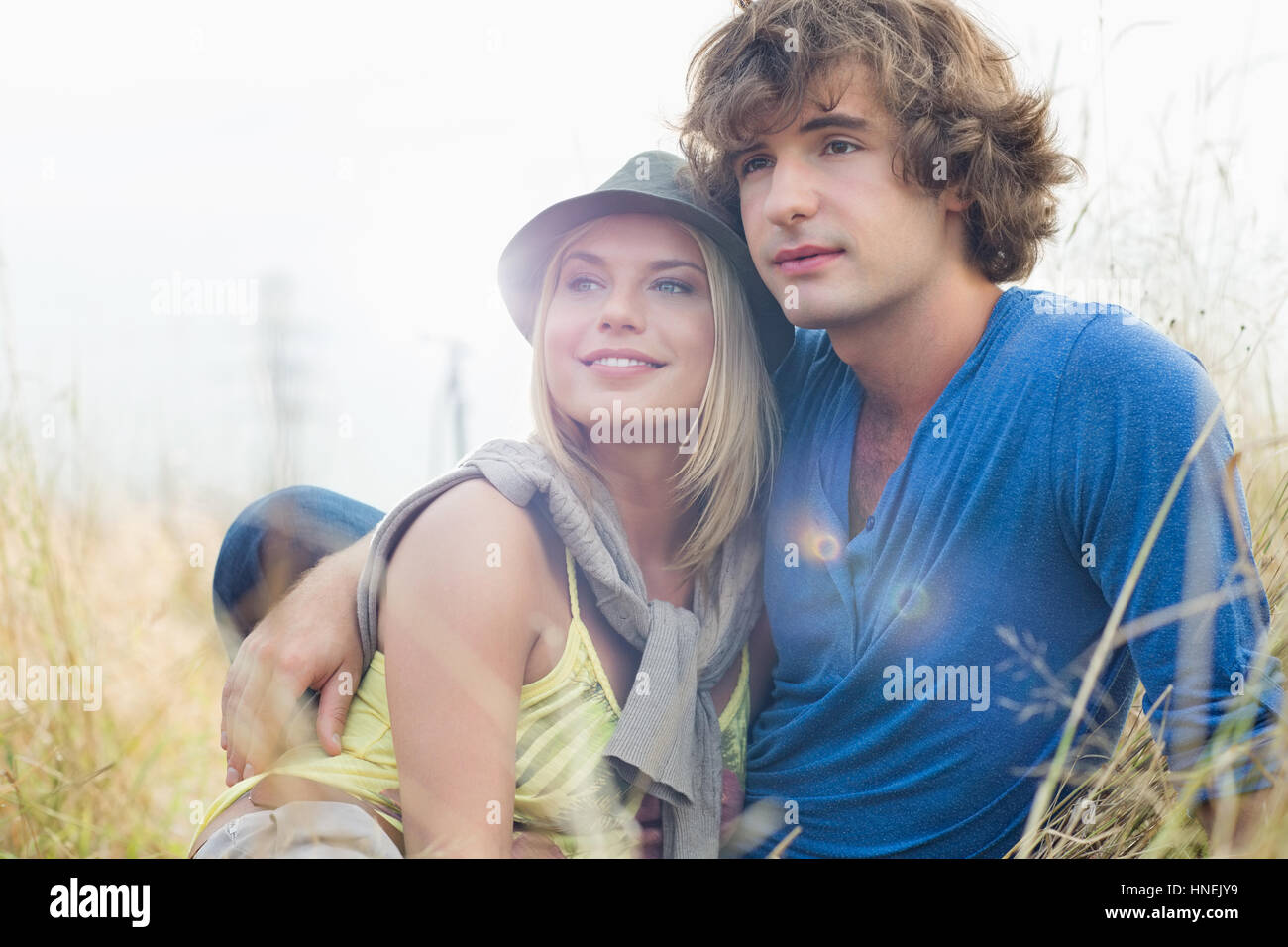 Romantic young couple looking away while sitting in field Stock Photo ...