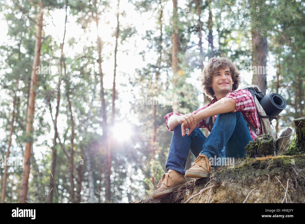 Full length of smiling male hiker looking away while sitting on cliff ...