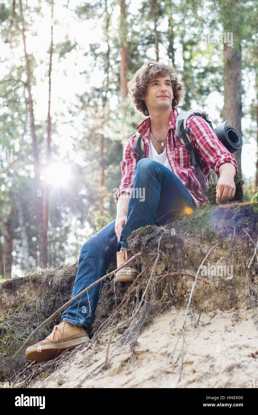 Full length of male hiker looking away while sitting on cliff in forest ...