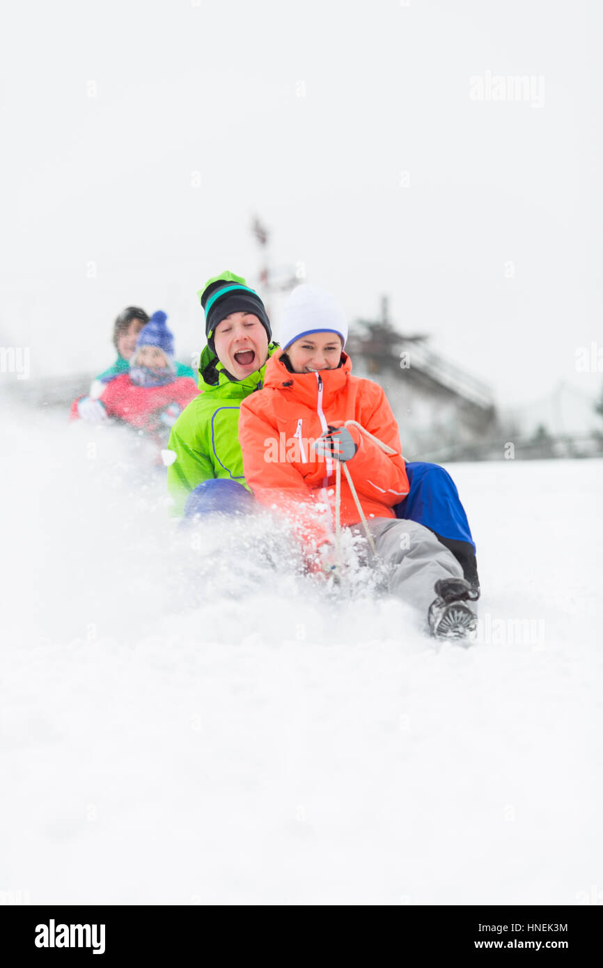 Excited young friends sledding in snow Stock Photo - Alamy