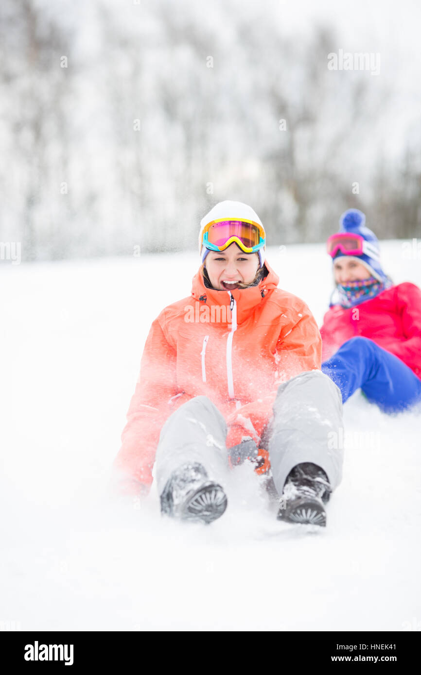 Young woman enjoying sled ride in snow with friend in background Stock ...