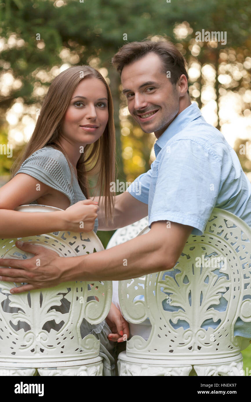 Portrait of smiling young couple sitting on chairs in park Stock Photo ...