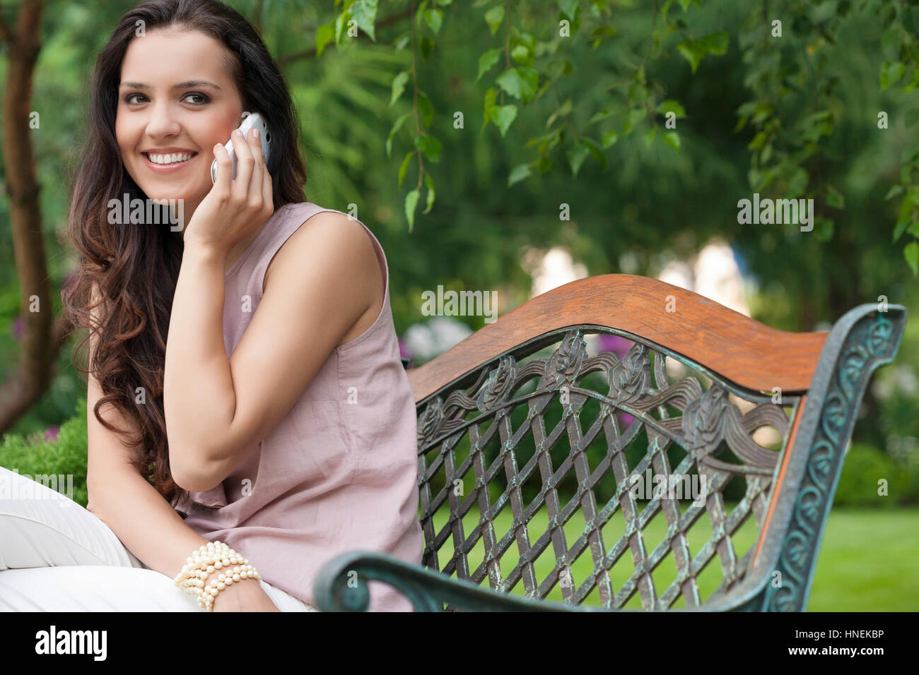 Beautiful young woman using cell phone on bench in park Stock Photo - Alamy