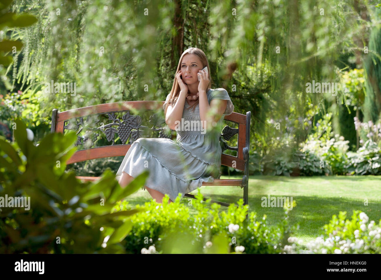 Tensed young woman using cell phone on bench in park Stock Photo - Alamy