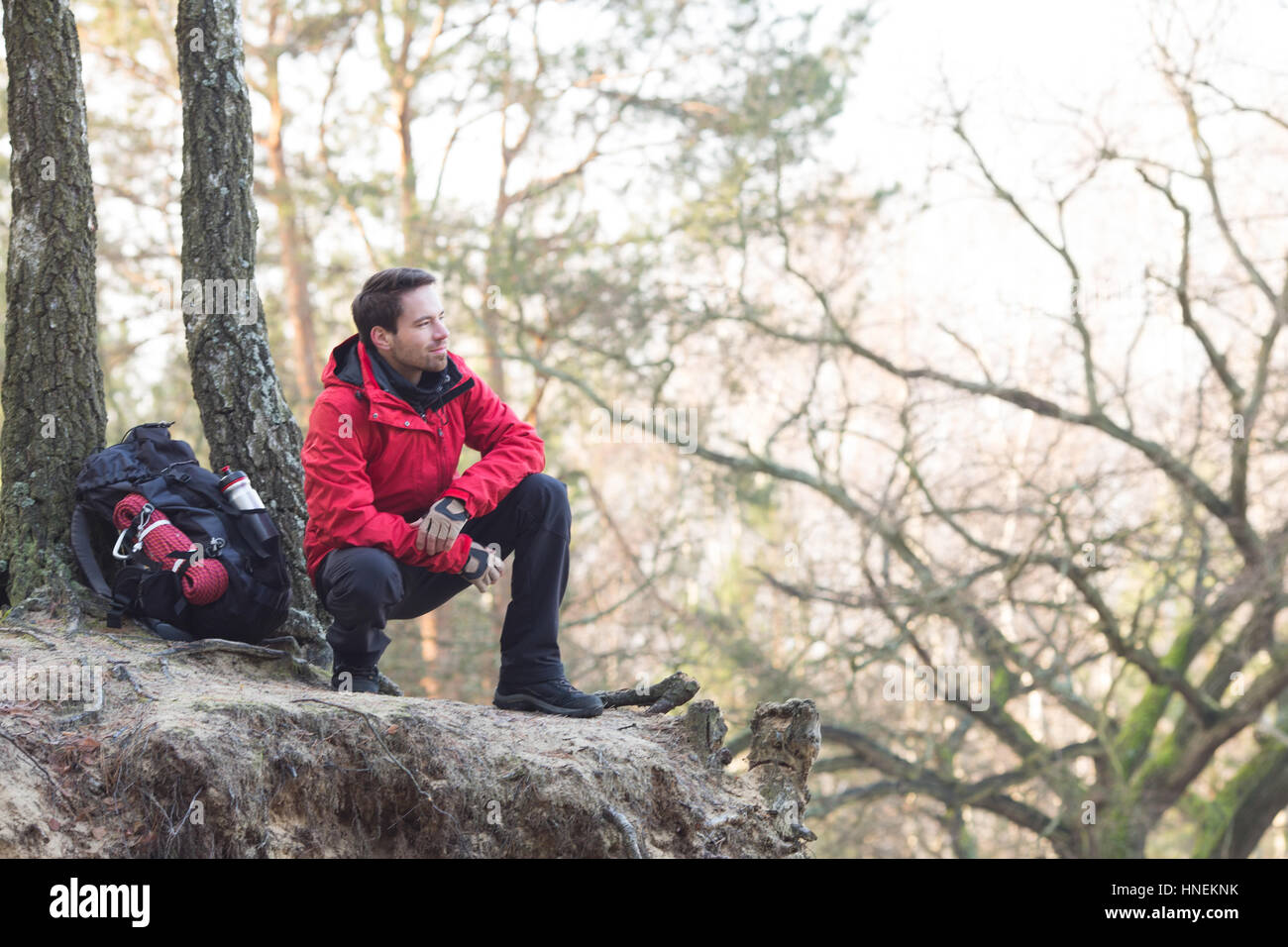 Full length of male hiker crouching on cliff in forest Stock Photo - Alamy