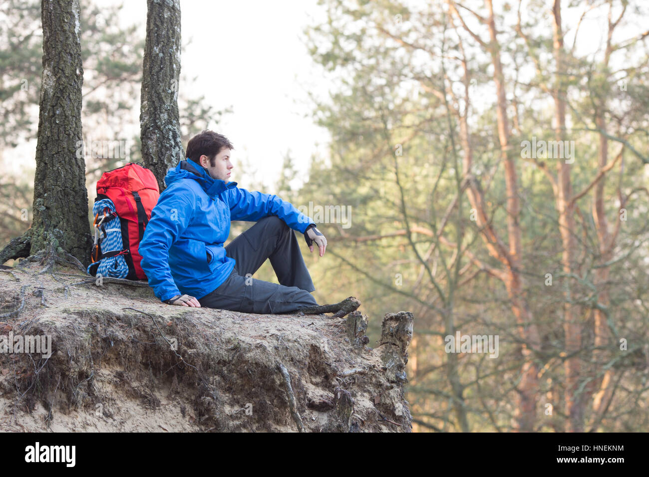 Side view of hiker sitting on edge of cliff in forest Stock Photo - Alamy