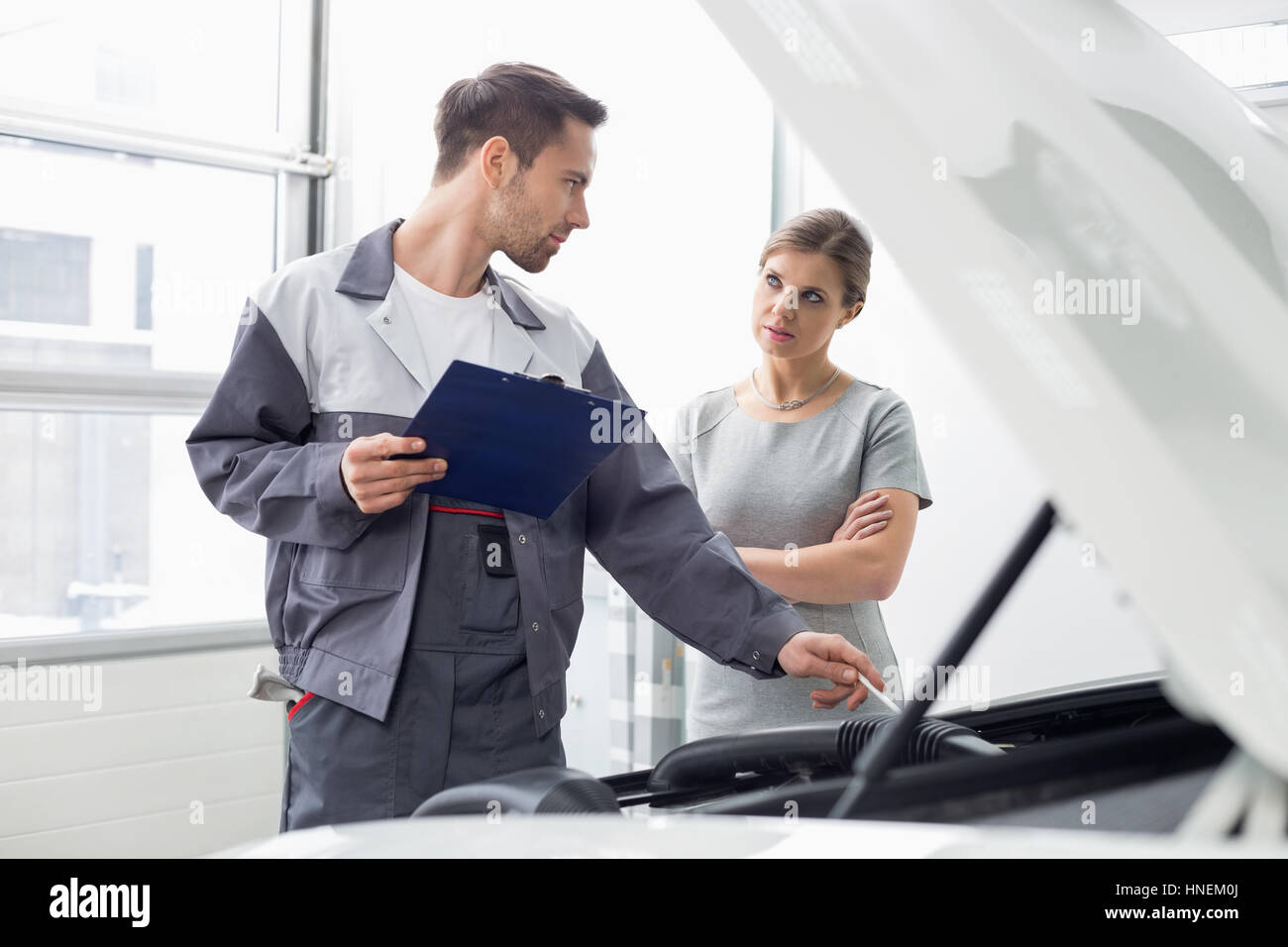 Young male engineer explaining car engine to female customer in ...