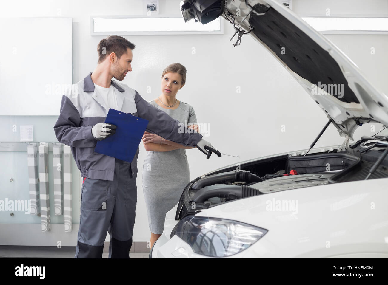 Young male repairman explaining car engine to female customer in ...