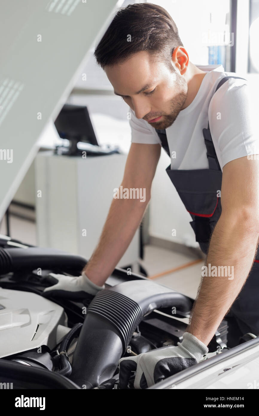 Full length side view of male mechanic examining car engine in repair ...