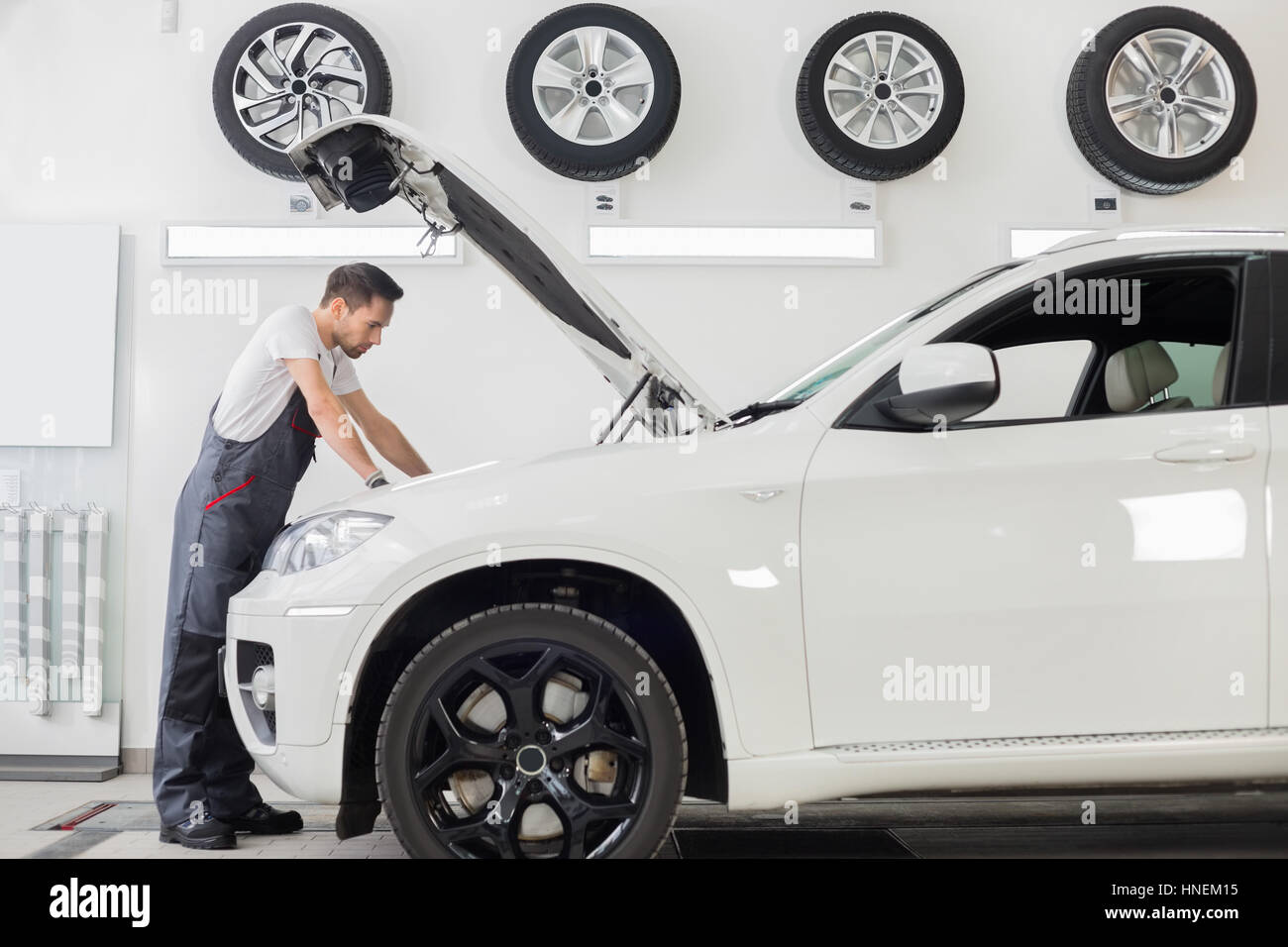 Full length side view of male mechanic examining car engine in repair ...