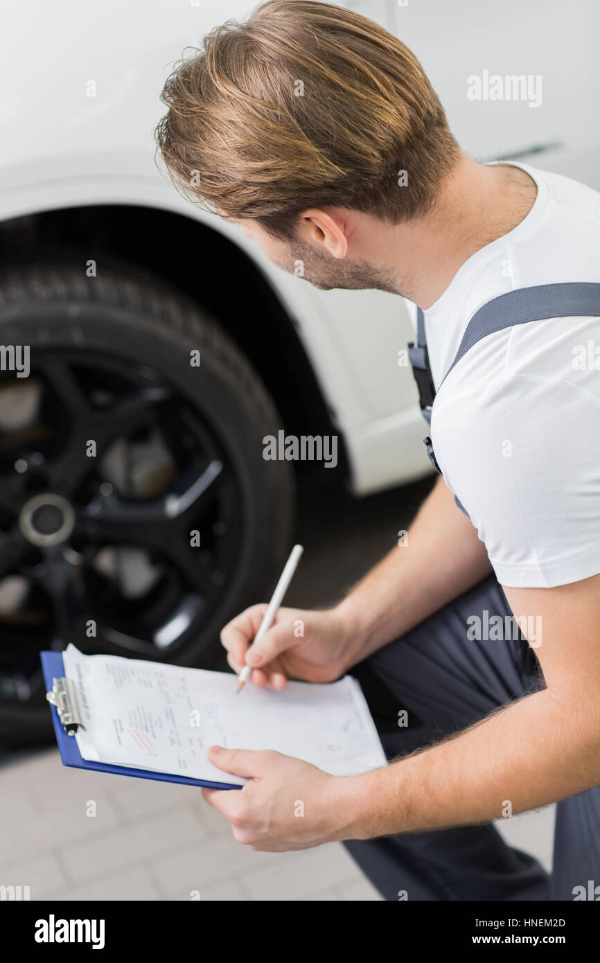 Side view of automobile mechanic writing on clipboard while examining ...