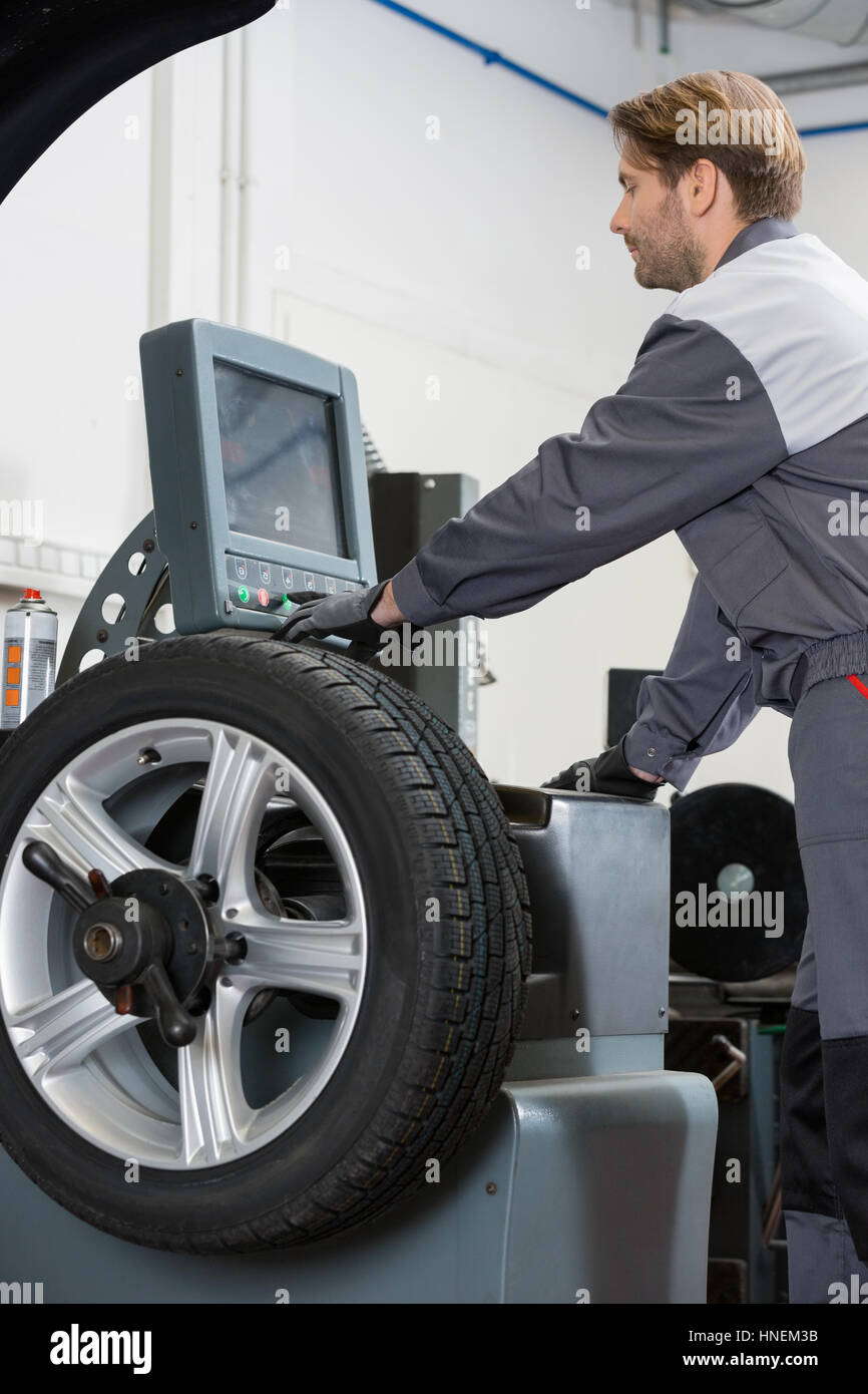 Side view of mid adult male mechanic repairing car's wheel in workshop ...