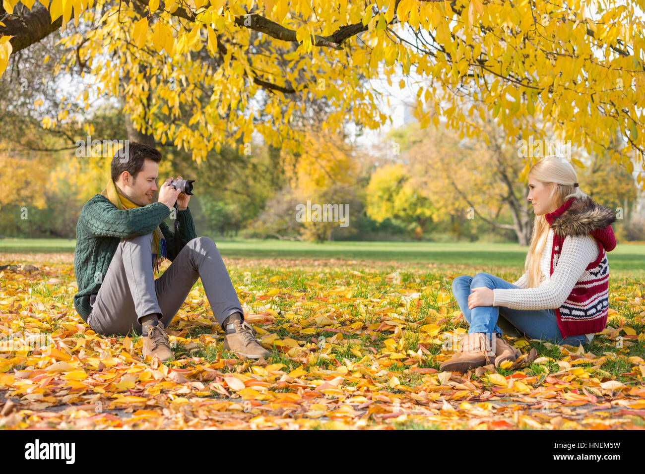 Full length of young man photographing woman in park during autumn ...