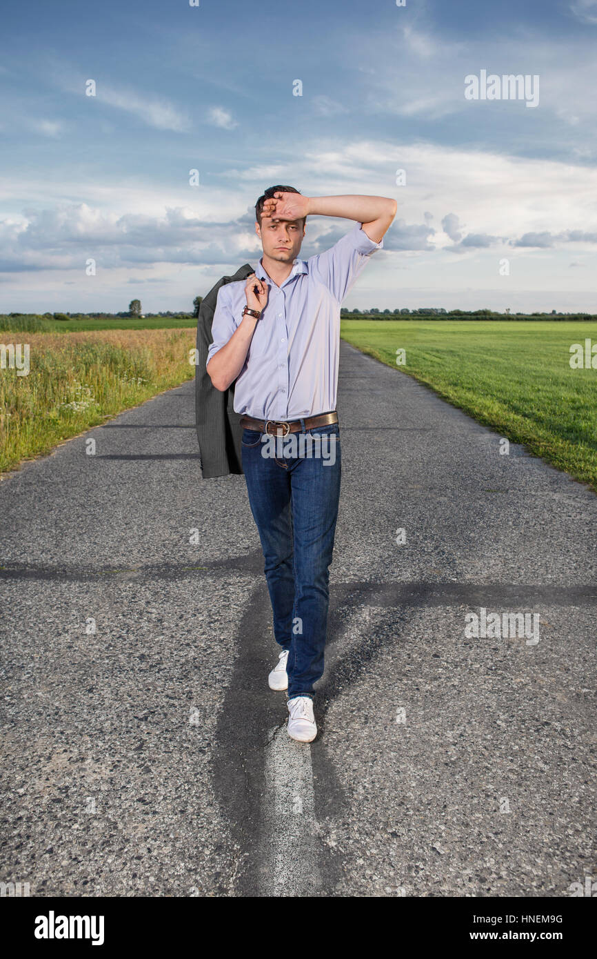 Full length of tired young man walking alone on rural road Stock Photo ...