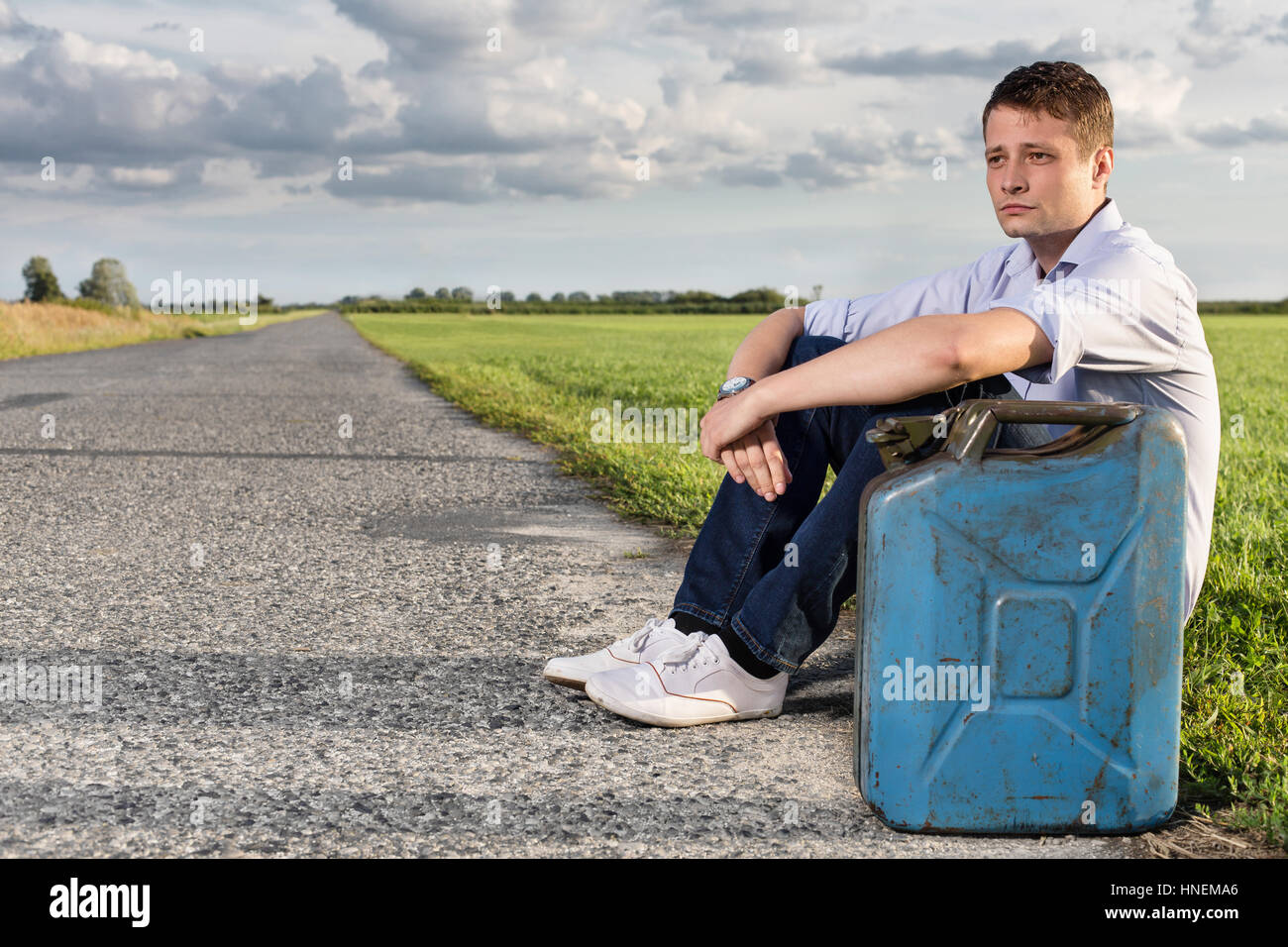 Full length of young man with empty gas can sitting by road Stock Photo ...