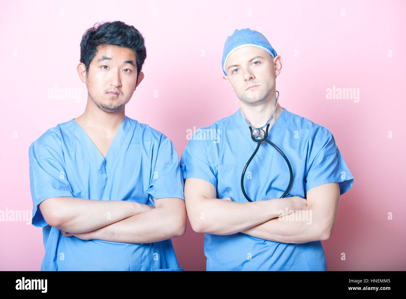Portrait of two male surgeons standing with arms crossed over pink ...