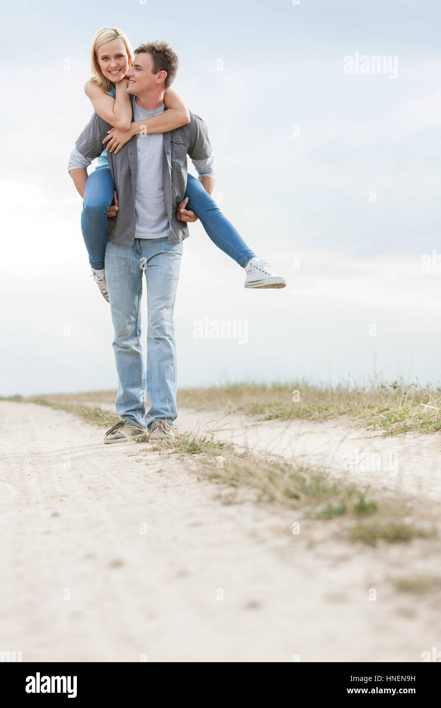 Happy young man giving piggyback ride to woman on trail at field Stock ...
