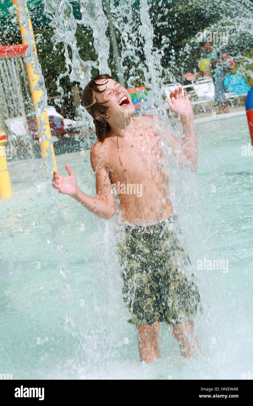 A teenaged boy stands under a water feature at a splash park Stock ...