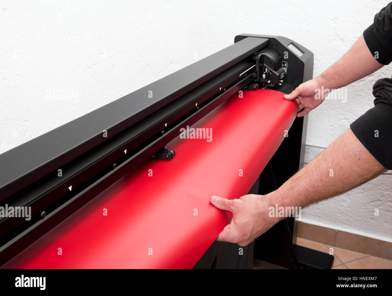 Hands of printing master loading red wide format film on plotter ...