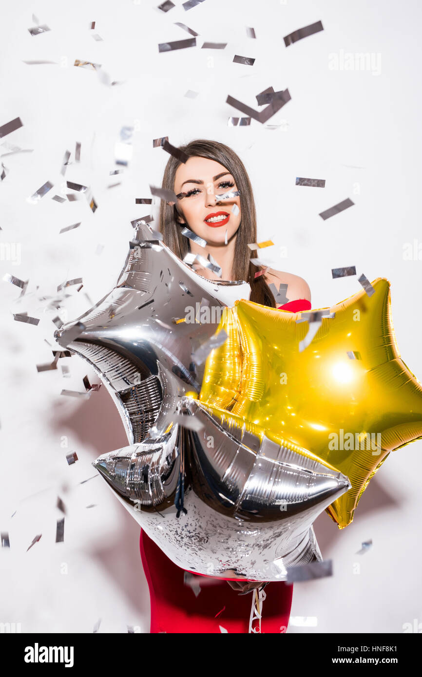 Young woman in red dress holding star balloon with fly confetti at ...