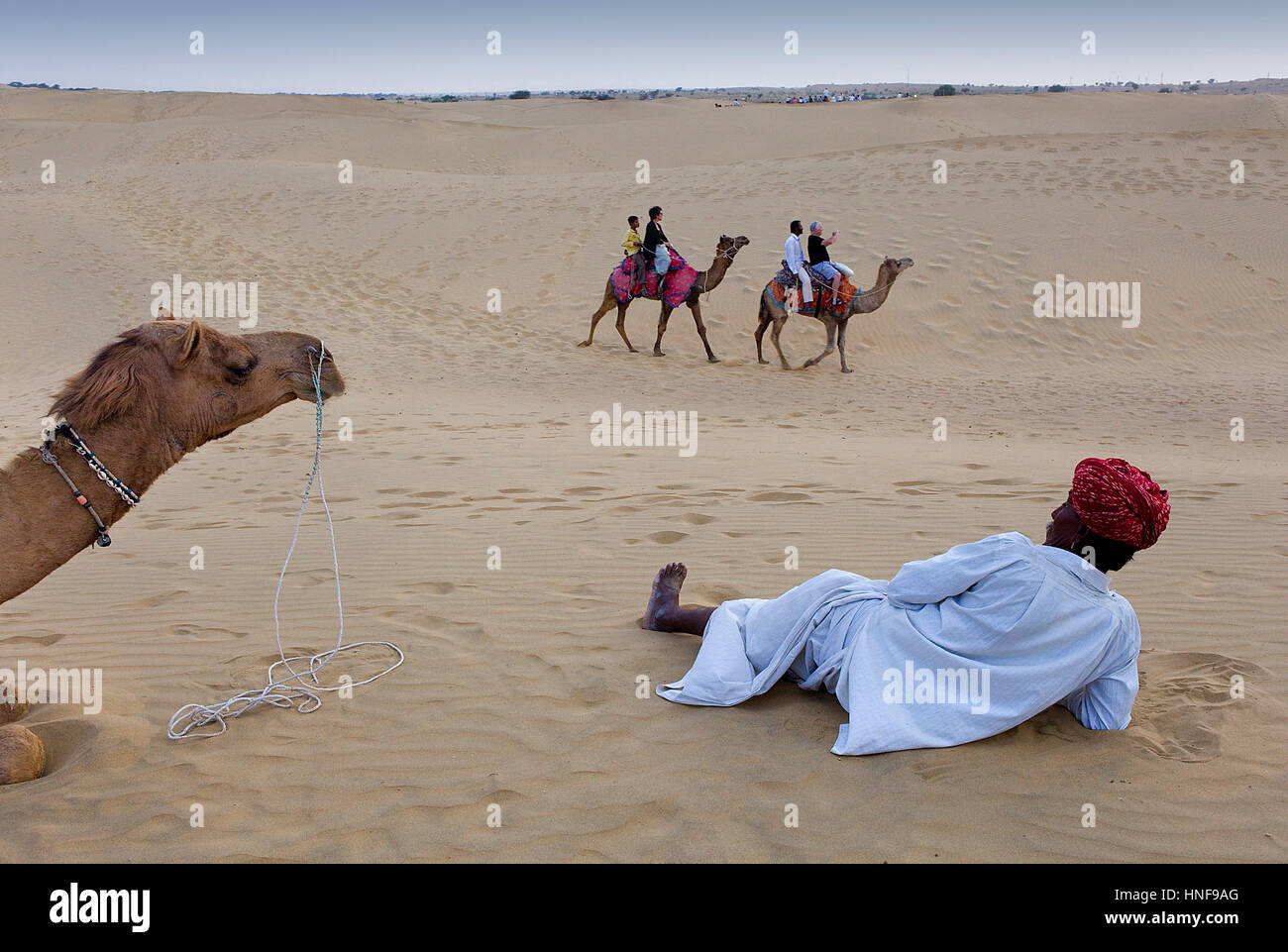 Native watching tourists riding camels on Sam dunes in Desert National ...