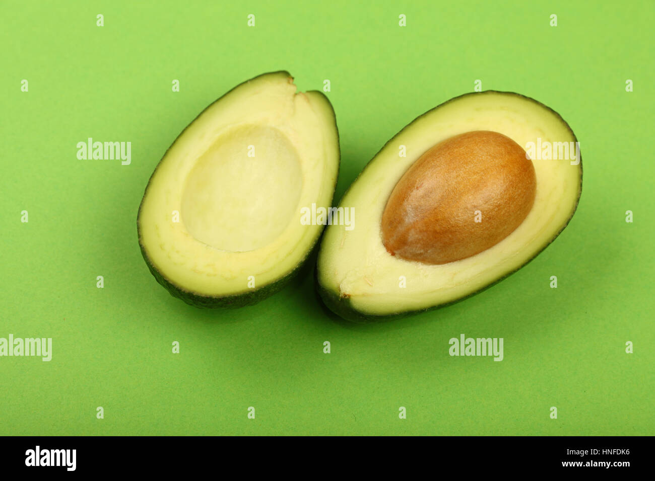 Two halves of one fresh ripe cut avocado with pit stone on green paper ...