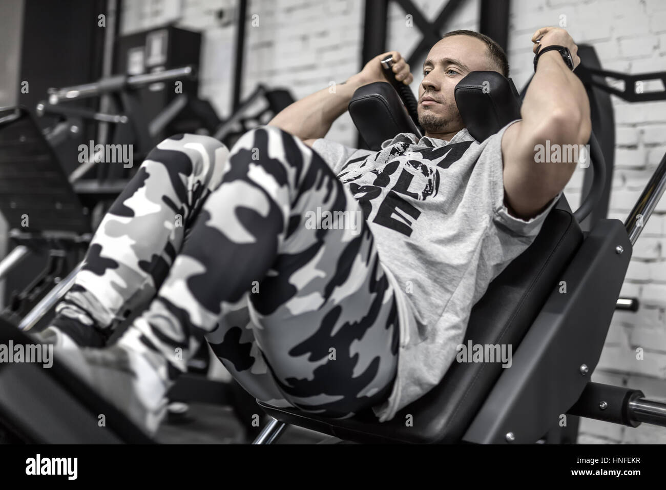 Mighty muscular man does leg press exercise on the trainer in the gym ...