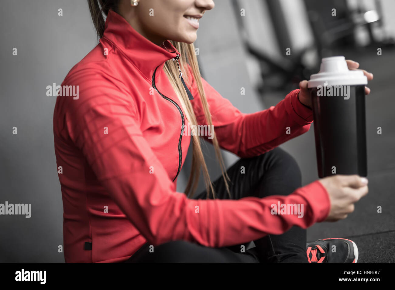 Calm smiling girl sits on the floor in the gym next to the gray wall ...