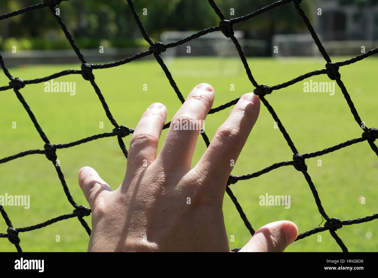 Man's hand extended to touch the mesh of a football field Stock Photo ...