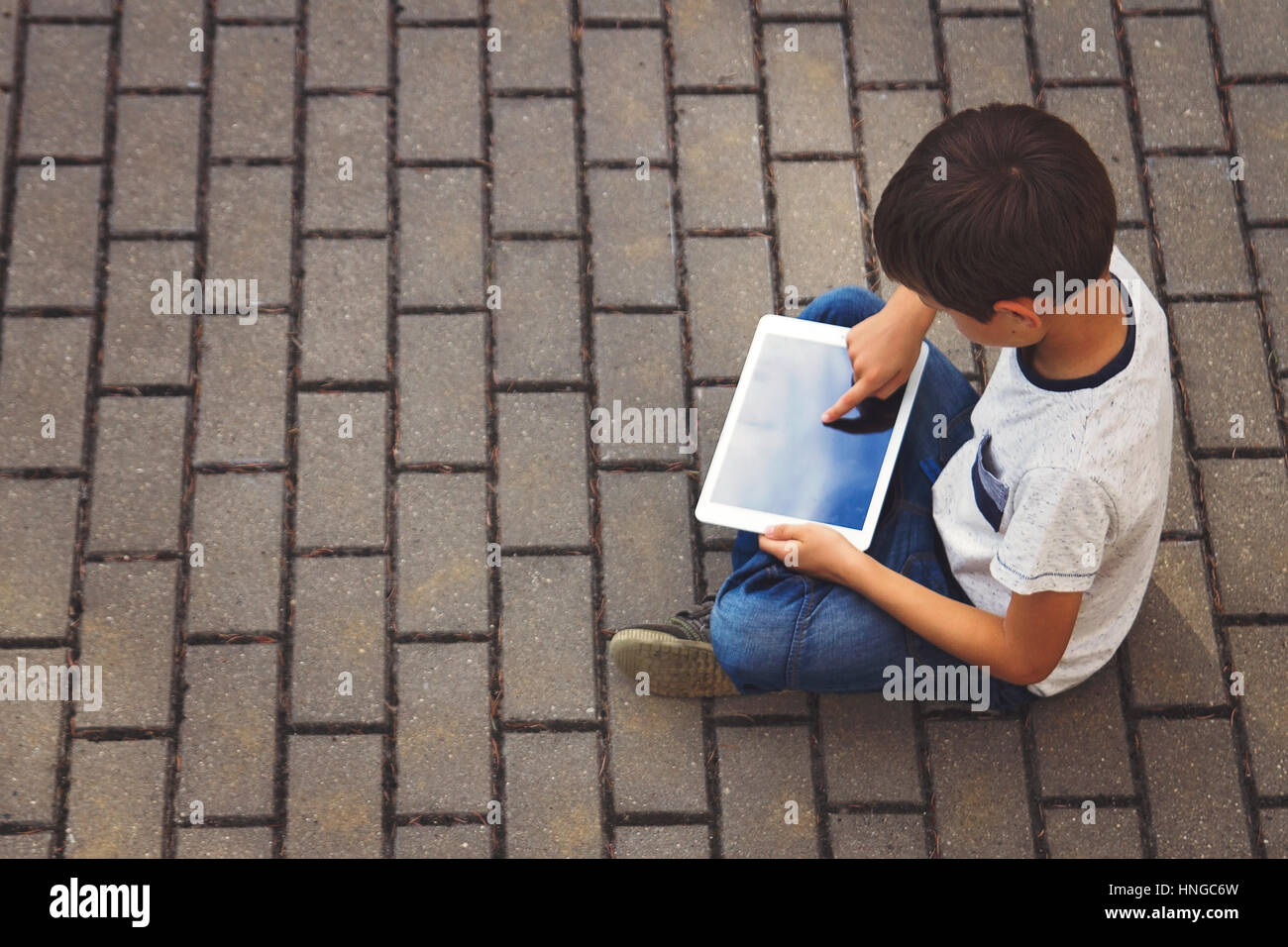 Child with tablet computer sitting on the pavement outdoors Stock Photo ...