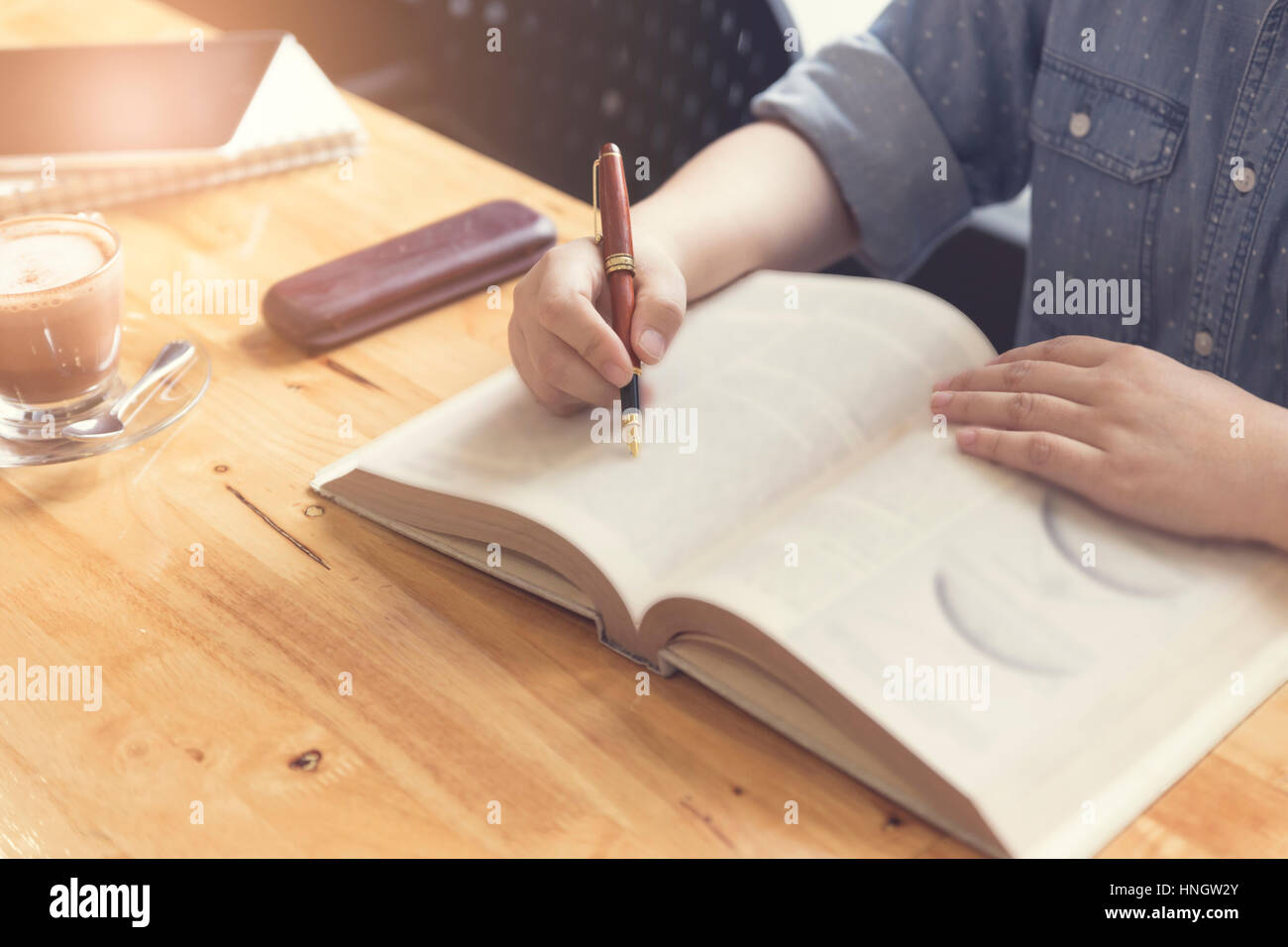 woman's hand reading book with pen, tablet and notebook on wooden table ...