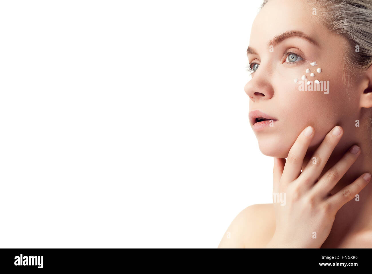 Beautiful woman with cream drops on face on white background in studio ...