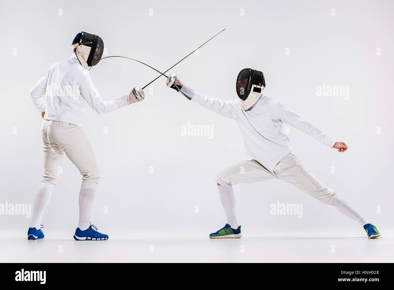 The two men wearing fencing suit practicing with sword against gray ...