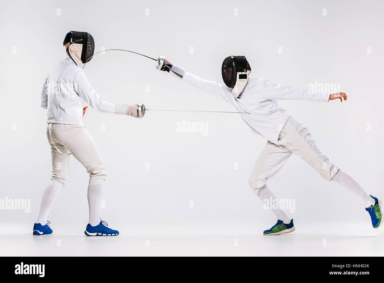 The two men wearing fencing suit practicing with sword against gray ...