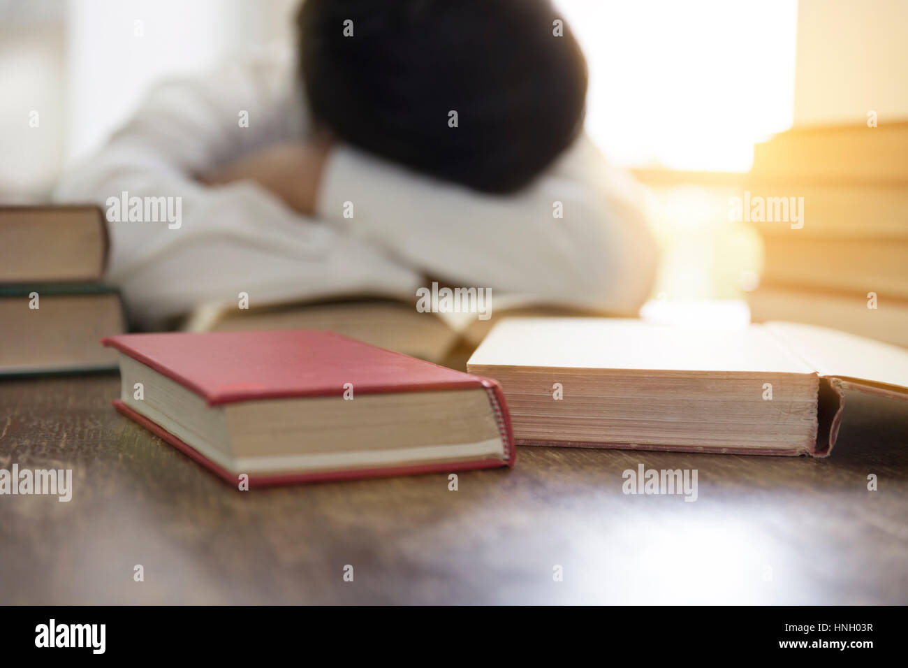 lazy man sleeping on book with textbook stack on wooden desk in library ...