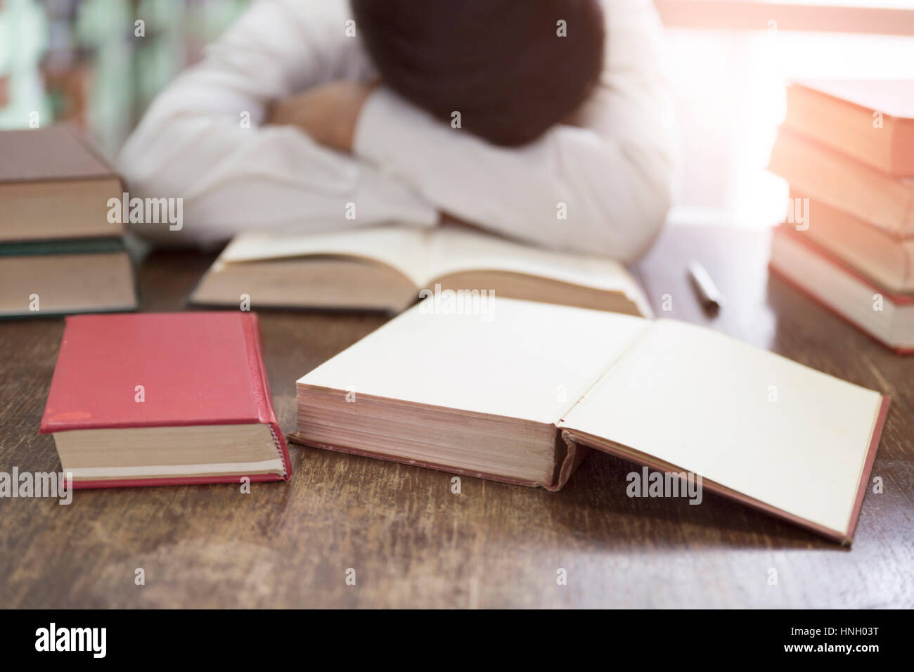 lazy man sleeping on book with textbook stack on wooden desk in library ...