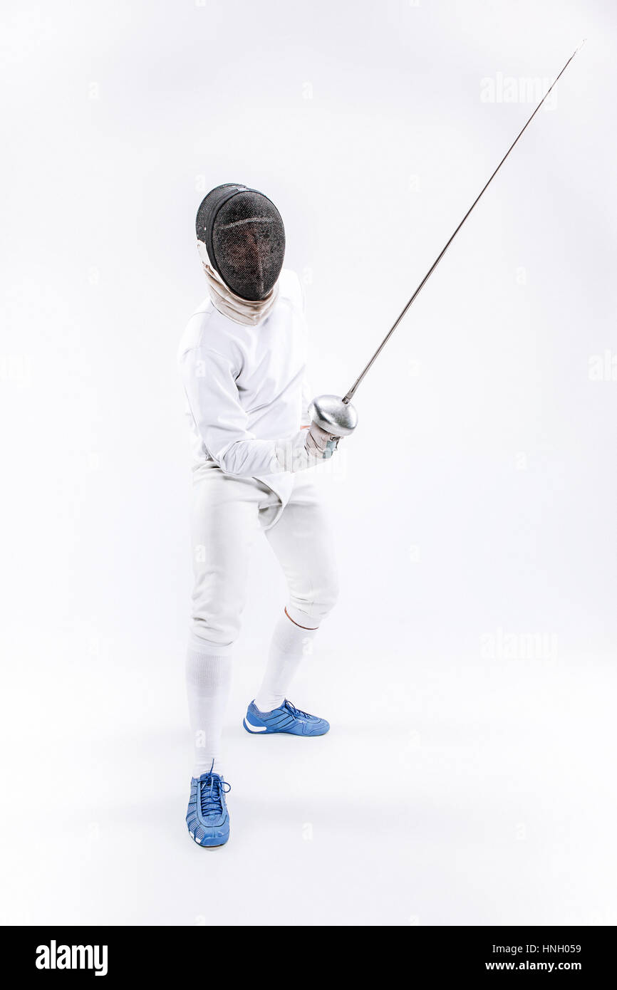 Man wearing fencing suit practicing with sword against gray studio ...