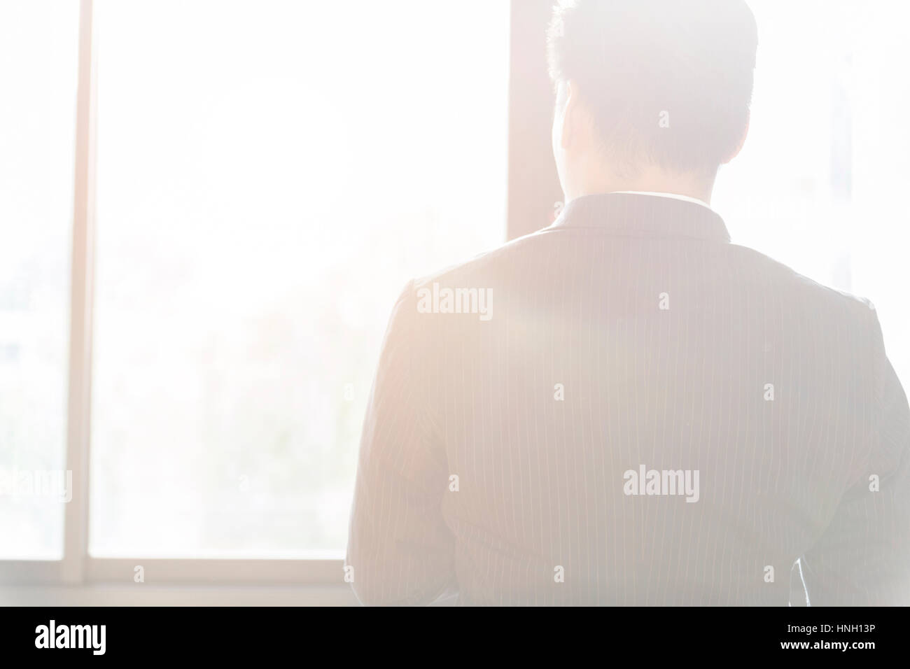 back of businessman in suit looking out through office window with ...